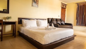 Quarto de hotel com uma cama grande, uma mesinha com uma planta, um sofá e um quadro na parede.