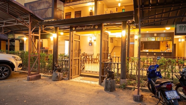 Restaurante tailandês tradicional com área de estar ao ar livre, escadaria que leva ao andar superior e uma motocicleta estacionada.