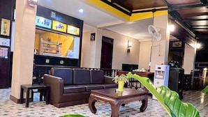 Um saguão de hotel com piso xadrez, um sofá, uma mesa de centro, uma planta em vaso e uma televisão.