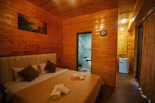 Quarto de cabana de madeira com cama, almofadas, relógio e uma pequena geladeira.