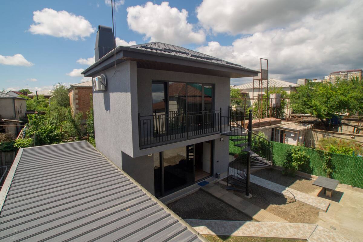 Uma casa moderna de dois andares com varanda, chaminé e quintal cercado.