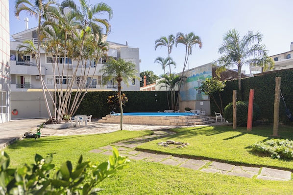 Um pátio com piscina, palmeiras e um edifício com varandas.