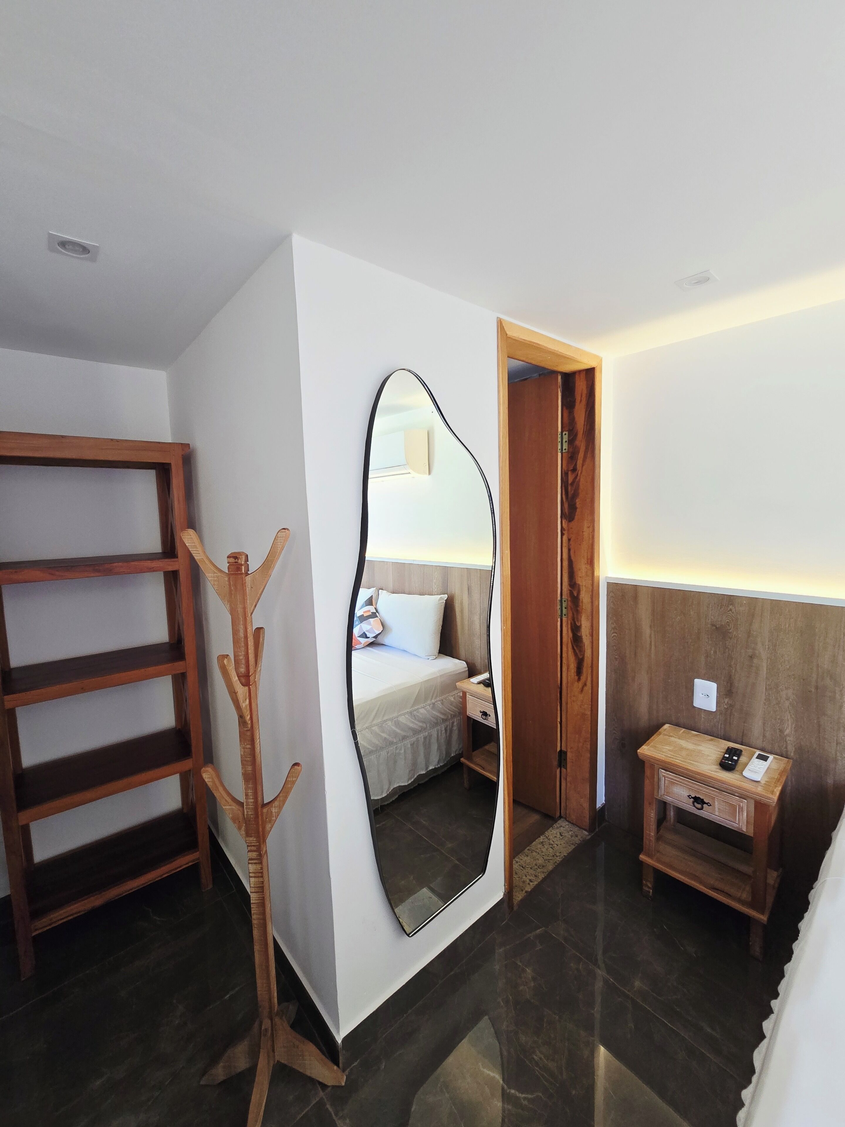 Quarto com cama, guarda-roupa de madeira, espelho, mesa de cabeceira e pequeno armário de madeira.