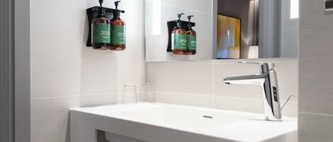 Casa de banho moderna com lavatório branco, torneira cromada e dois dispensadores de sabonete verde fixados na parede.