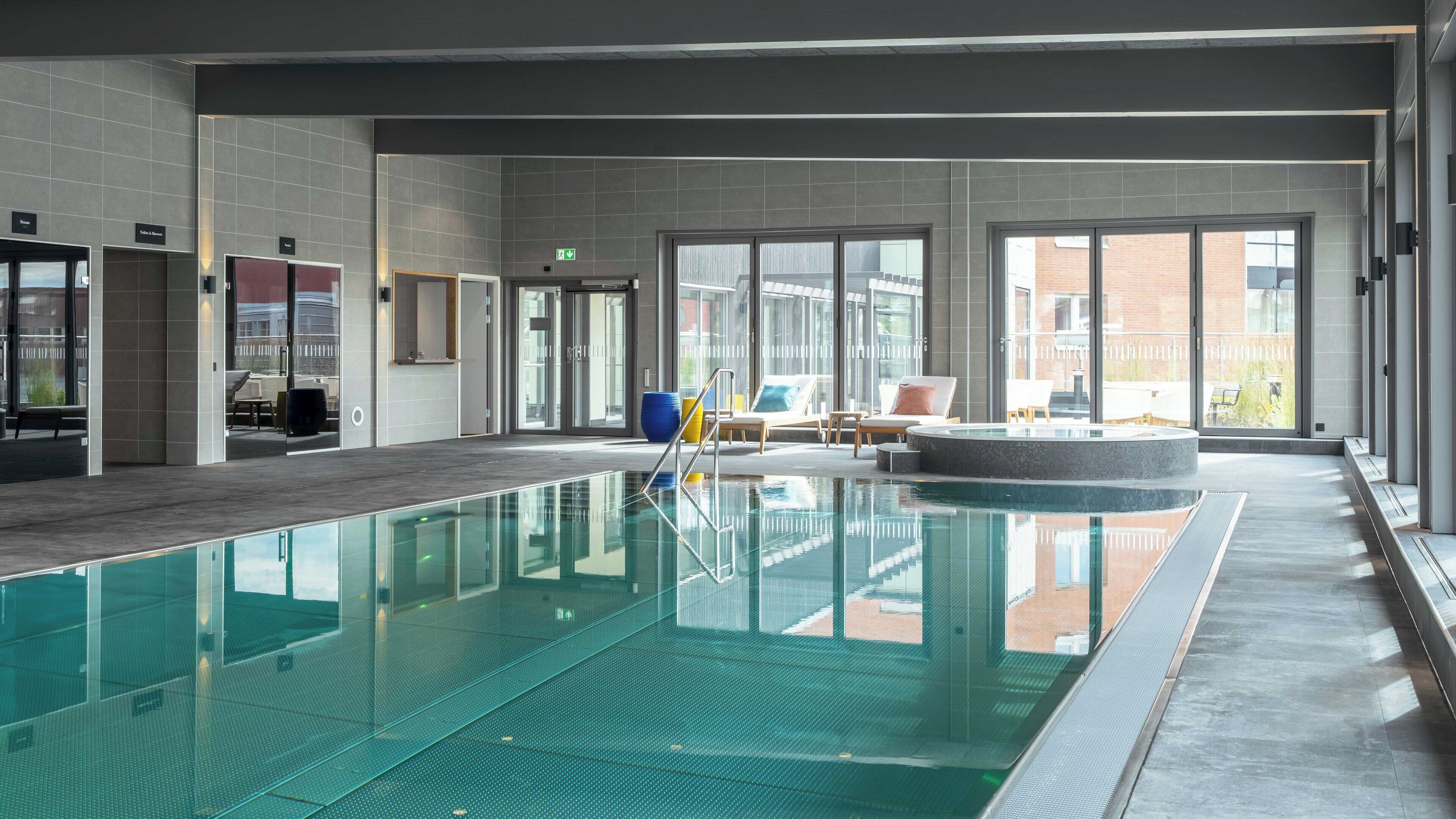 Piscina interior com água cristalina, rodeada por espreguiçadeiras e um solário.