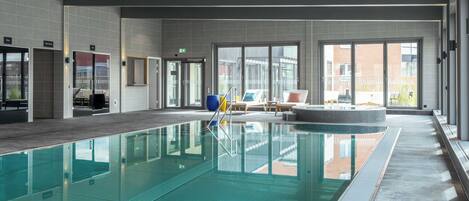 Piscina interior com água cristalina, rodeada por espreguiçadeiras e um solário.