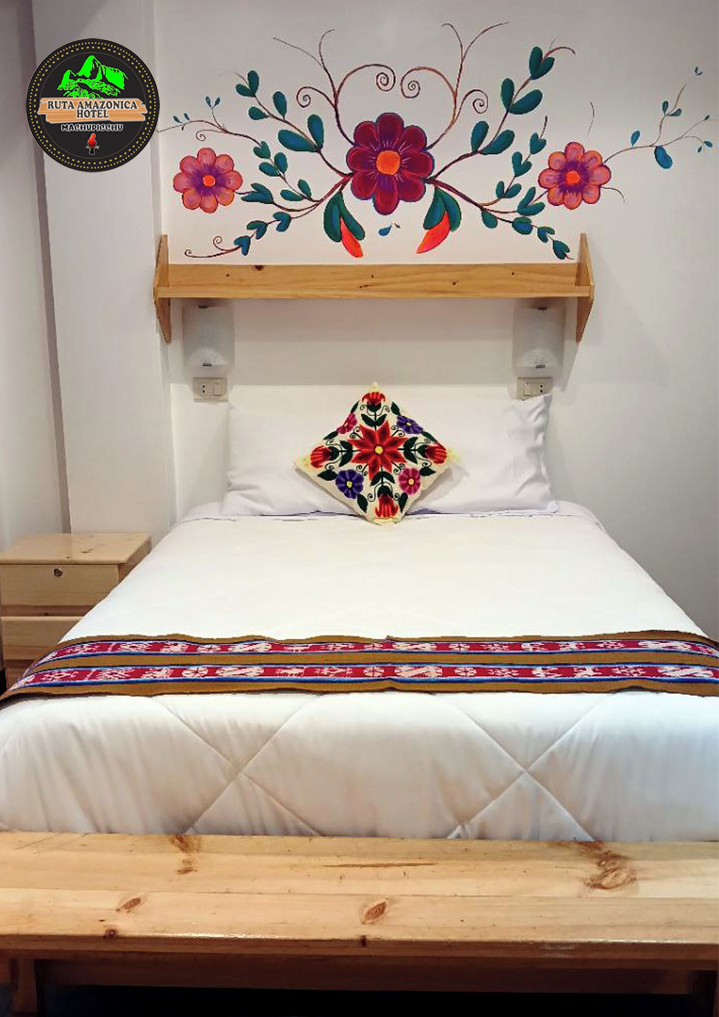Quarto de hotel com uma cama, cabeceira de madeira, mesa de cabeceira e um objeto decorativo na parede acima da cama.