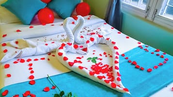 Uma cama com toalha em formato de cisne, pétalas de rosa vermelhas e balões.