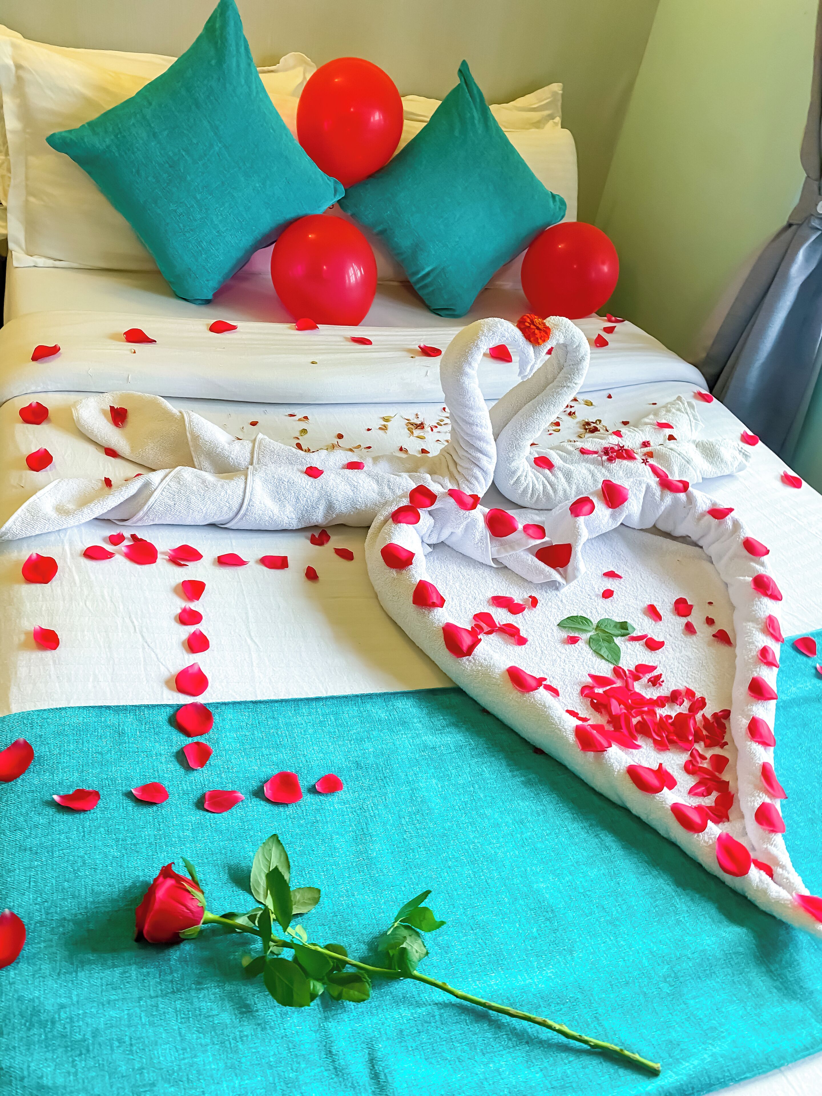 Uma cama bem arrumada com lençóis brancos, pétalas de rosa vermelhas e um arranjo de toalha em formato de cisne.