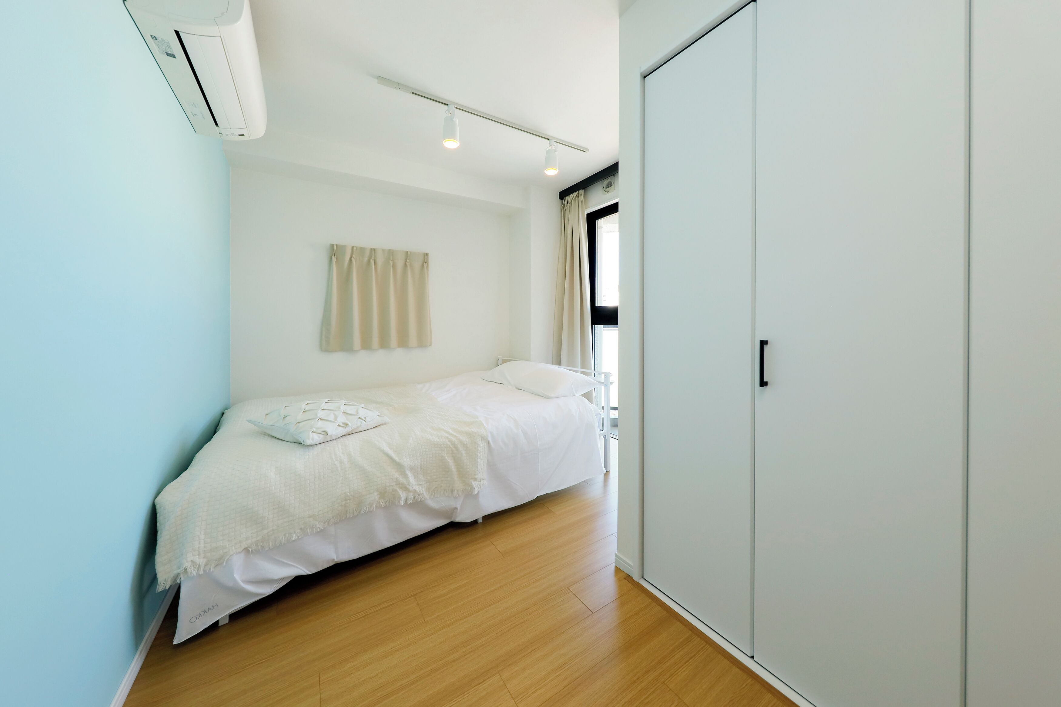 Um quarto com uma cama de solteiro, um guarda-roupa, uma janela com cortinas e um aparelho de ar condicionado.