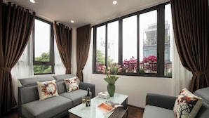 Uma sala de estar moderna com um sofá cinza, uma mesa de centro e vista para um edifício com flores cor-de-rosa.