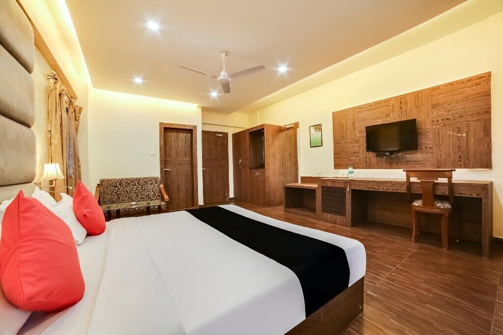 Quarto de hotel com uma cama grande, uma escrivaninha com televisão, painéis de madeira e um ventilador de teto.