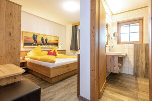 Quarto com cama de madeira, pintura de caminhantes, mesa de cabeceira de madeira e um banco de madeira.