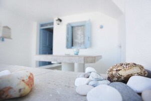 Uma mesa de pedra com um pão e pedrinhas, uma parede branca e uma janela com moldura azul.