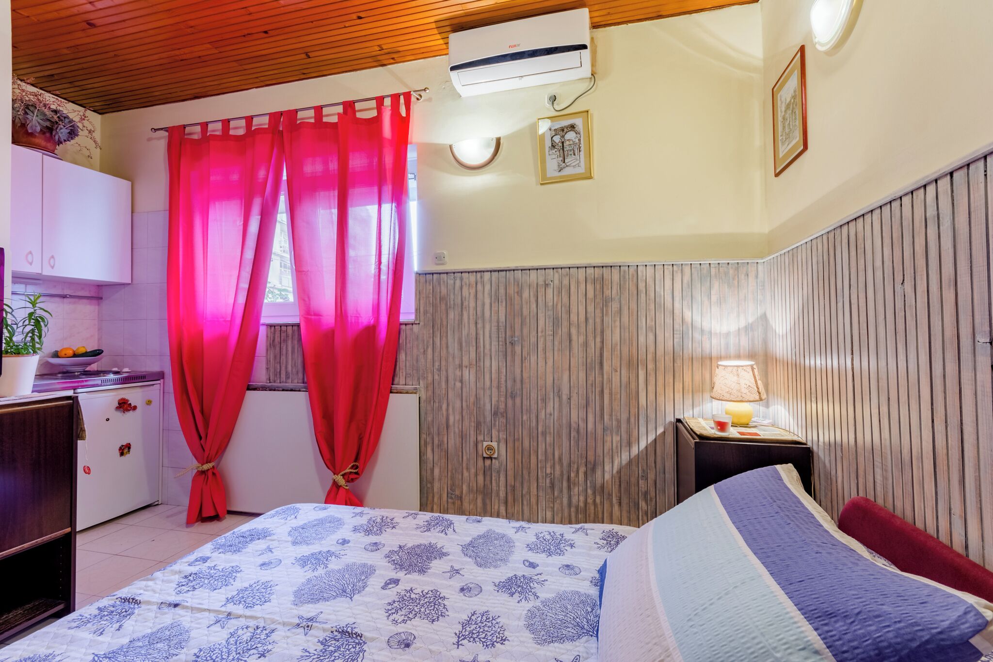 Quarto com cama, mesa de cabeceira, luminária, guarda-roupa e janela com cortinas vermelhas.