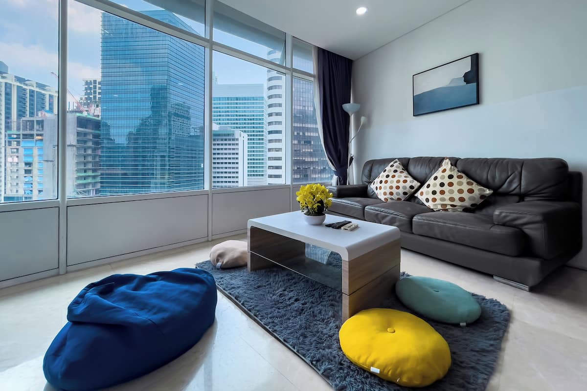 Uma sala de estar moderna com uma janela ampla, um sofá, uma mesa de centro e um puff azul.
