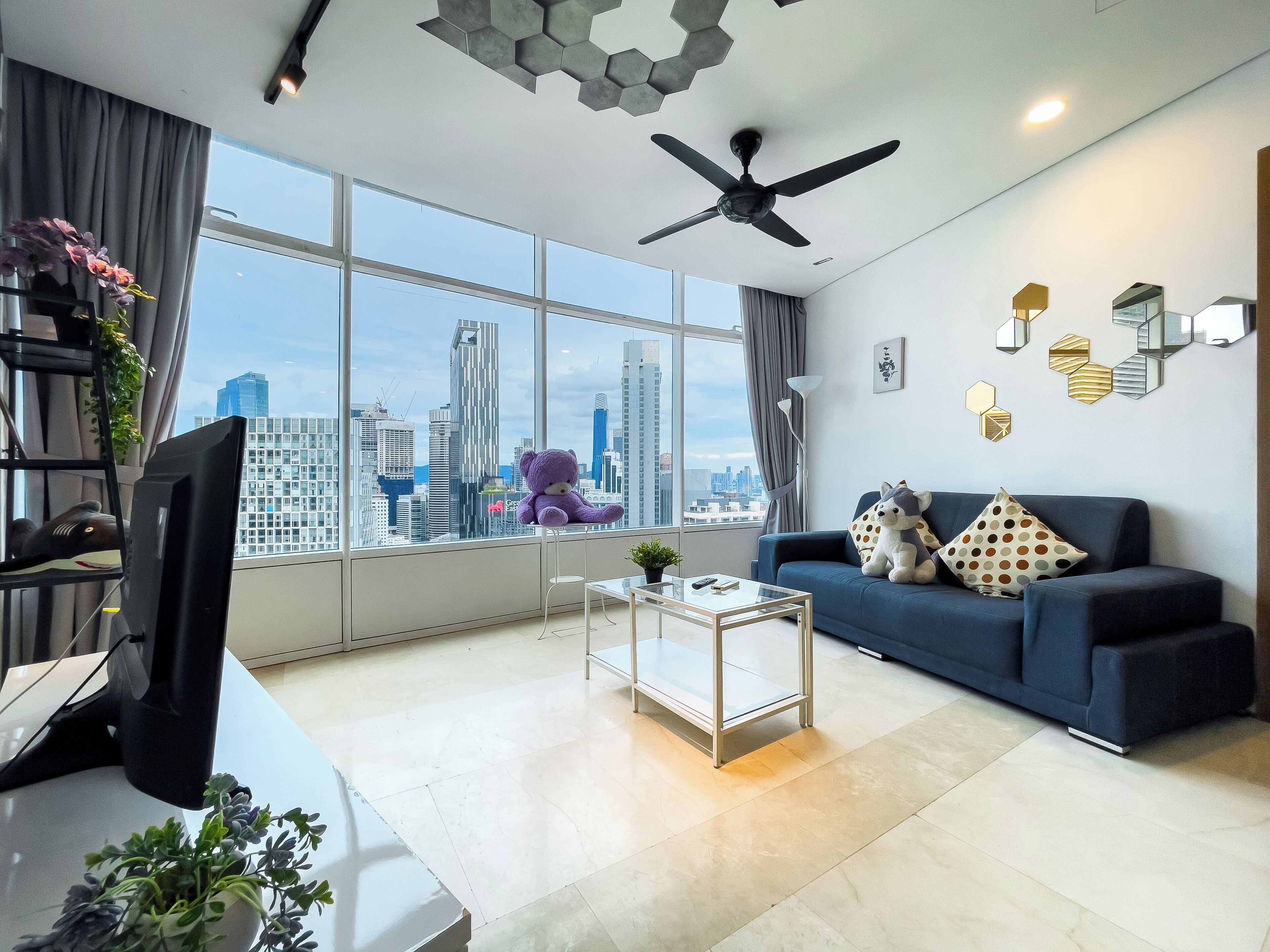 Uma sala de estar moderna com vista para a cidade, um ventilador de teto e um sofá azul com almofadas decorativas.