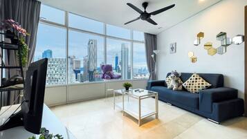 Uma sala de estar moderna com vista para a cidade, um ventilador de teto e um sofá azul com almofadas decorativas.