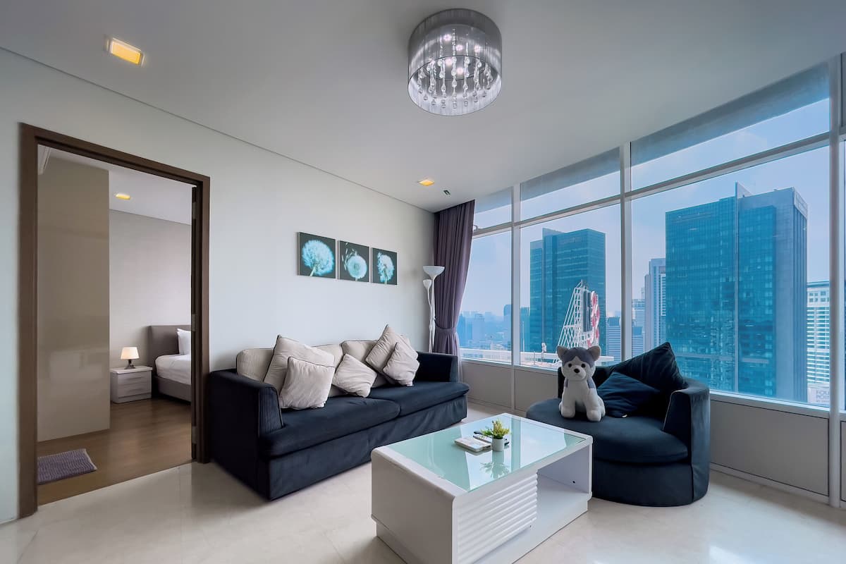 Uma sala de estar moderna com um sofá, uma mesa de centro e vista para prédios da cidade.