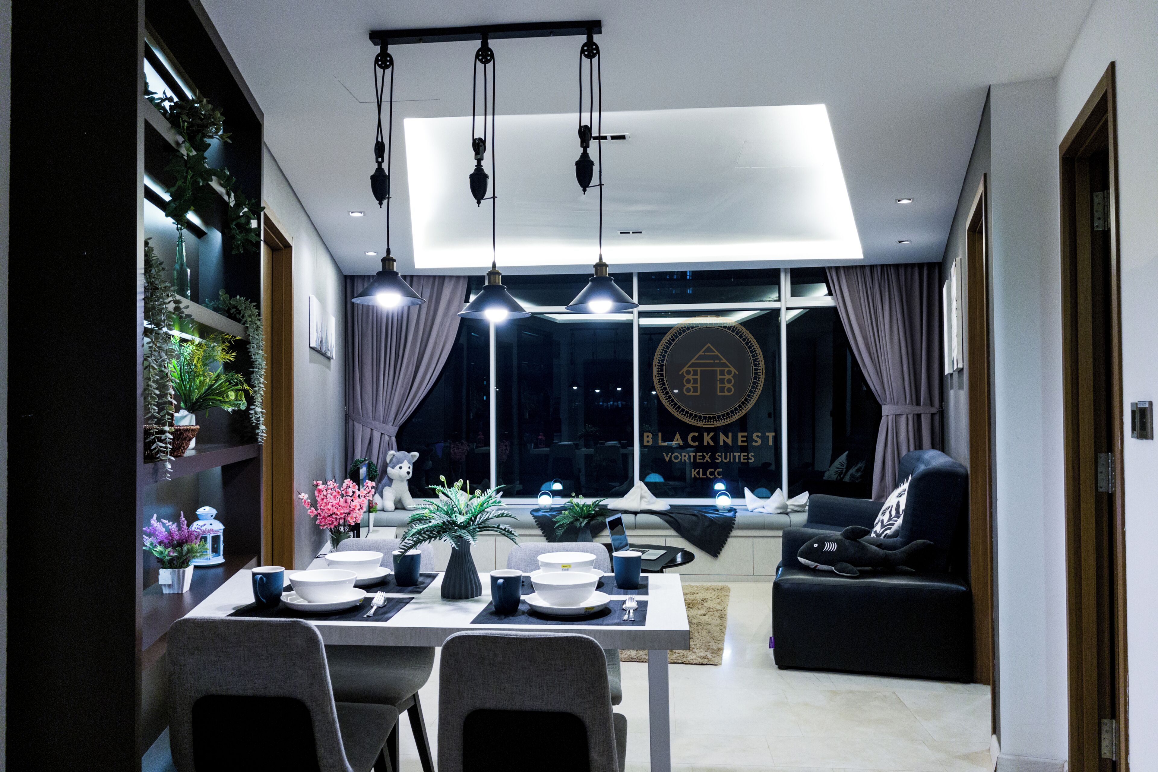 Uma área de refeições moderna com uma mesa posta para quatro pessoas, um sofá e uma janela com cortinas.