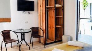 Quarto moderno com cama, duas cadeiras de vime, uma mesa pequena, TV e um guarda-roupa de madeira.