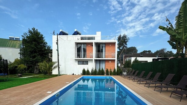 Um edifício moderno com piscina, cercado por um deque de madeira e espreguiçadeiras.