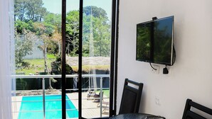 Quarto com porta de vidro para piscina, televisão na parede e duas cadeiras.