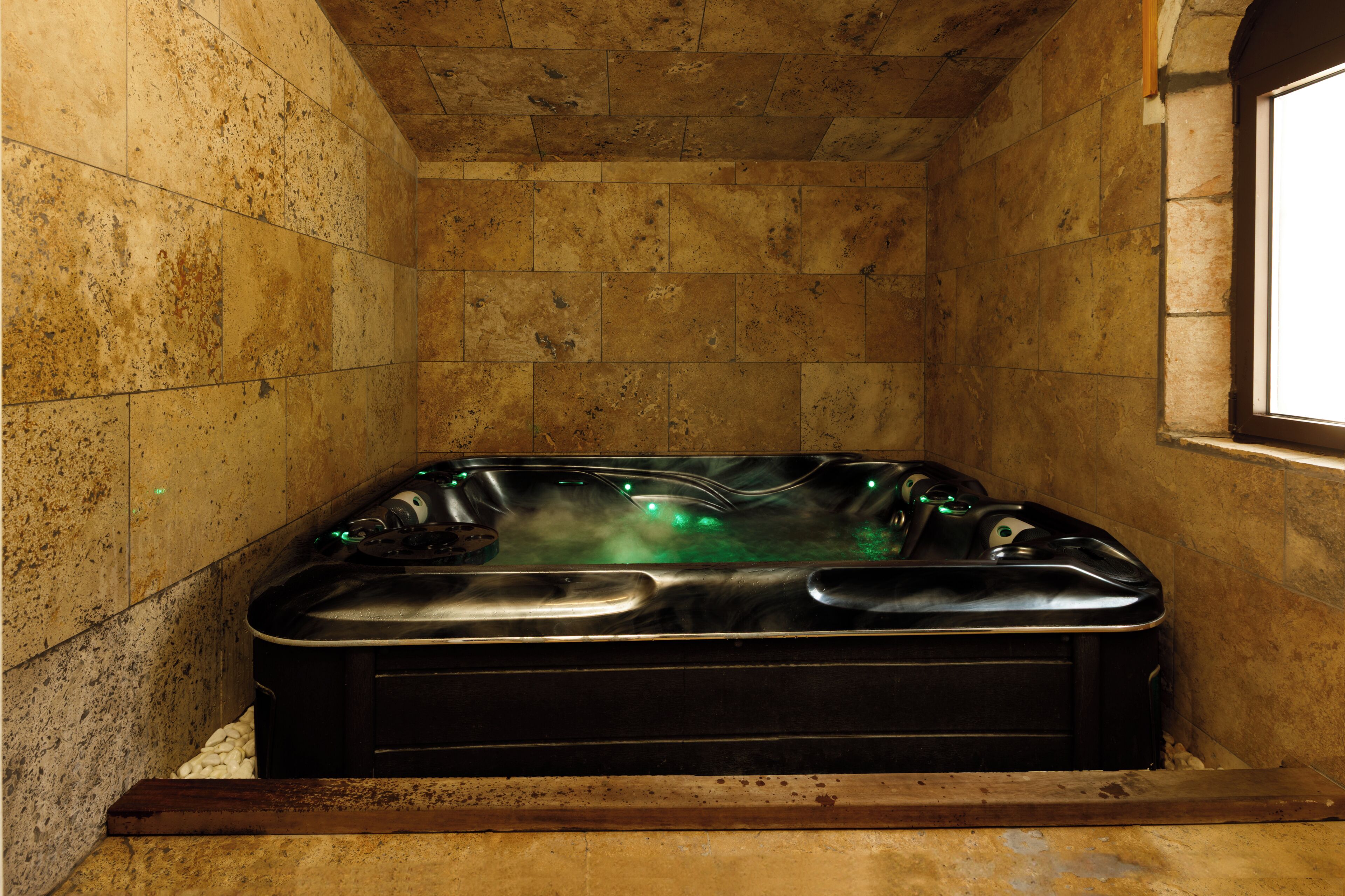 Uma banheira de hidromassagem em um espaço com paredes de pedra e uma janela à direita.