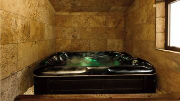 Uma banheira de hidromassagem em um espaço com paredes de pedra e uma janela à direita.