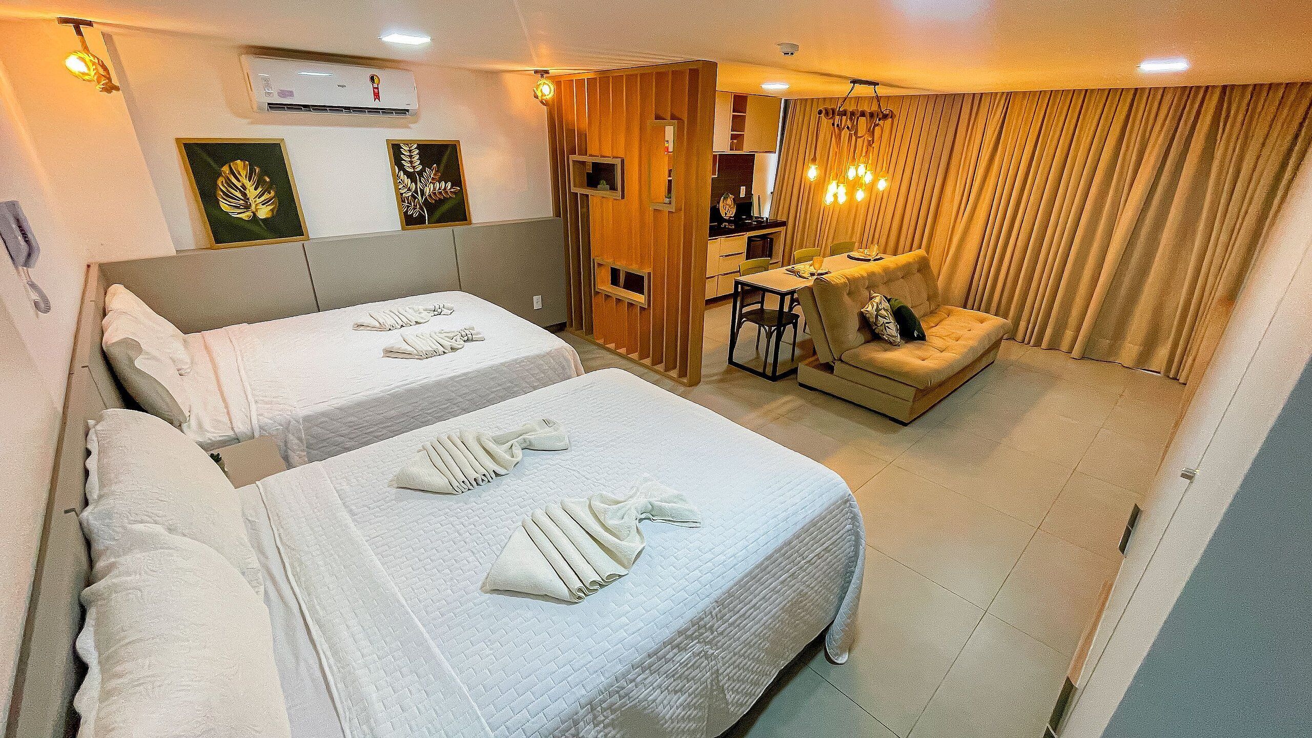 Quarto de hotel com duas camas, um sofá, uma mesinha e um espelho.
