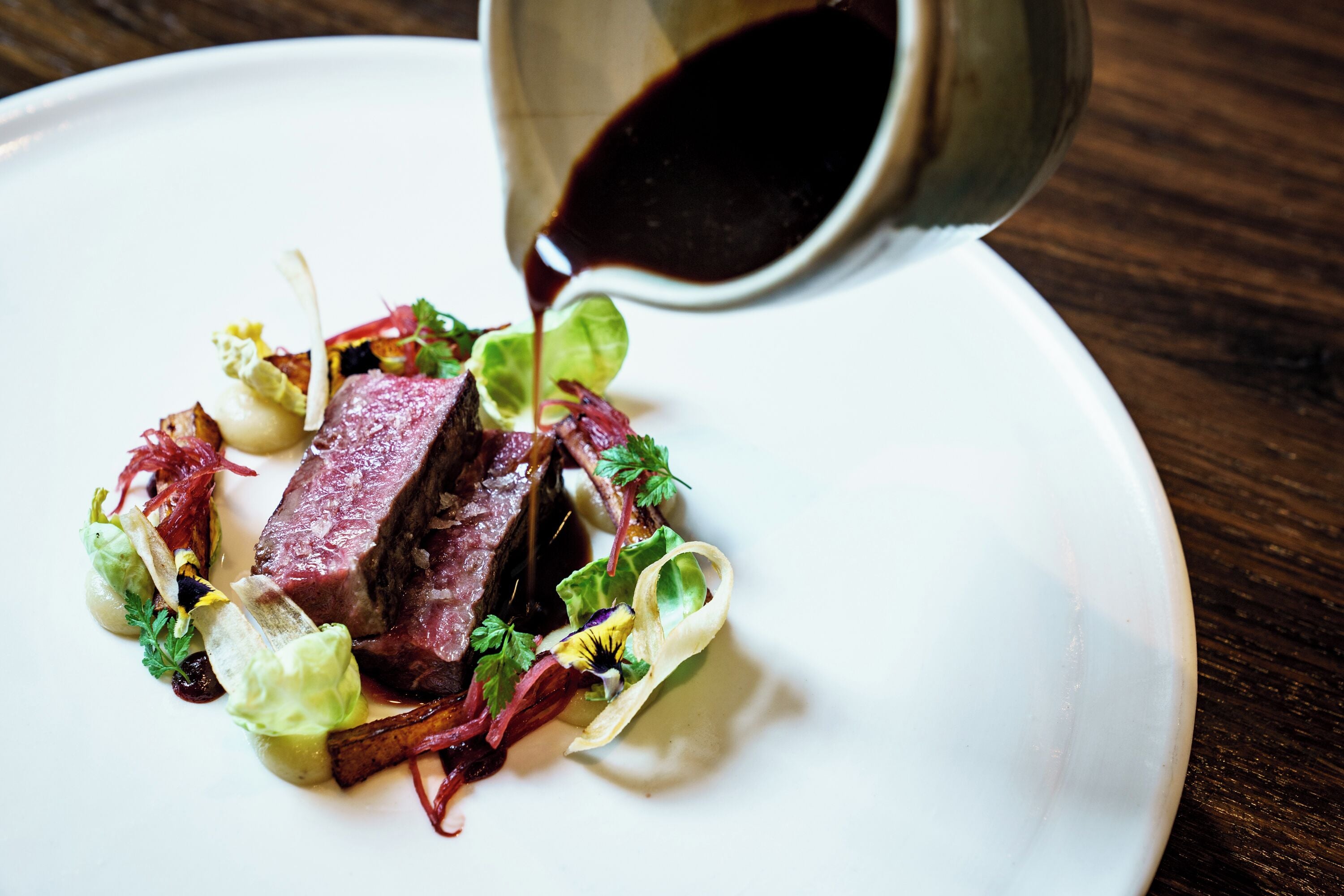 Prato branco com bife, legumes e molho.