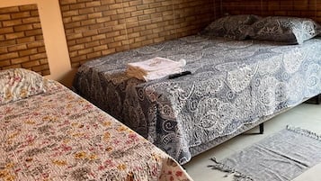 Quarto com duas camas, cabeceira de tijolos e janela com grades.