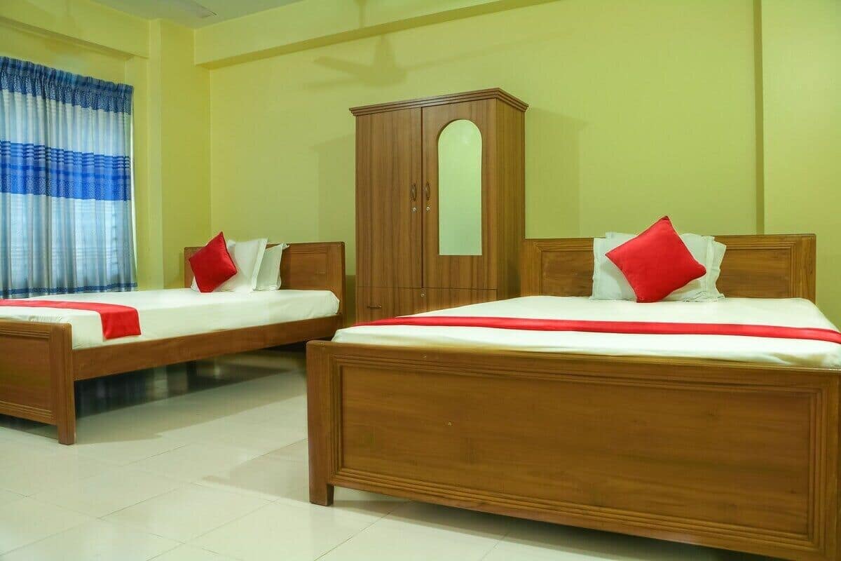 Duas camas de madeira com roupa de cama vermelha e branca, um guarda-roupa de madeira e uma janela com cortinas azuis.