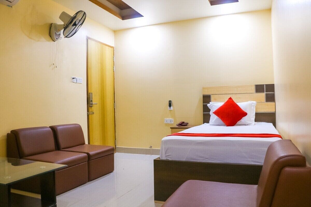 Quarto de hotel com cama, sofá, mesinha e ventilador.