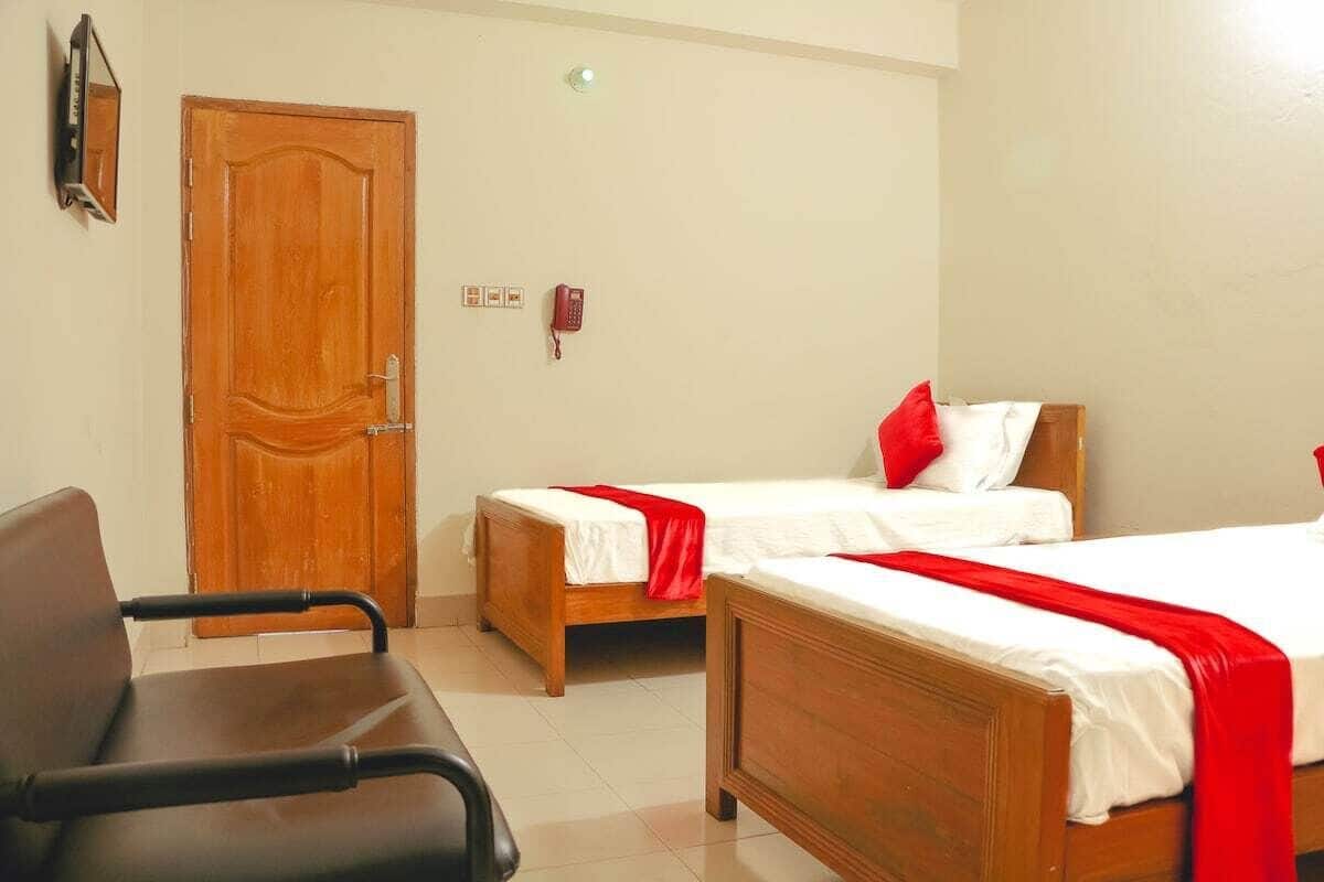 Quarto com duas camas de madeira, uma cadeira de madeira, uma porta e um telefone fixado na parede.