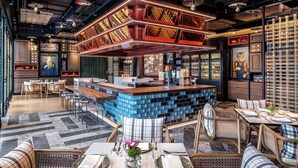 Uma área de bar moderna com balcão central, diferentes opções de assentos e diversos equipamentos de bar.