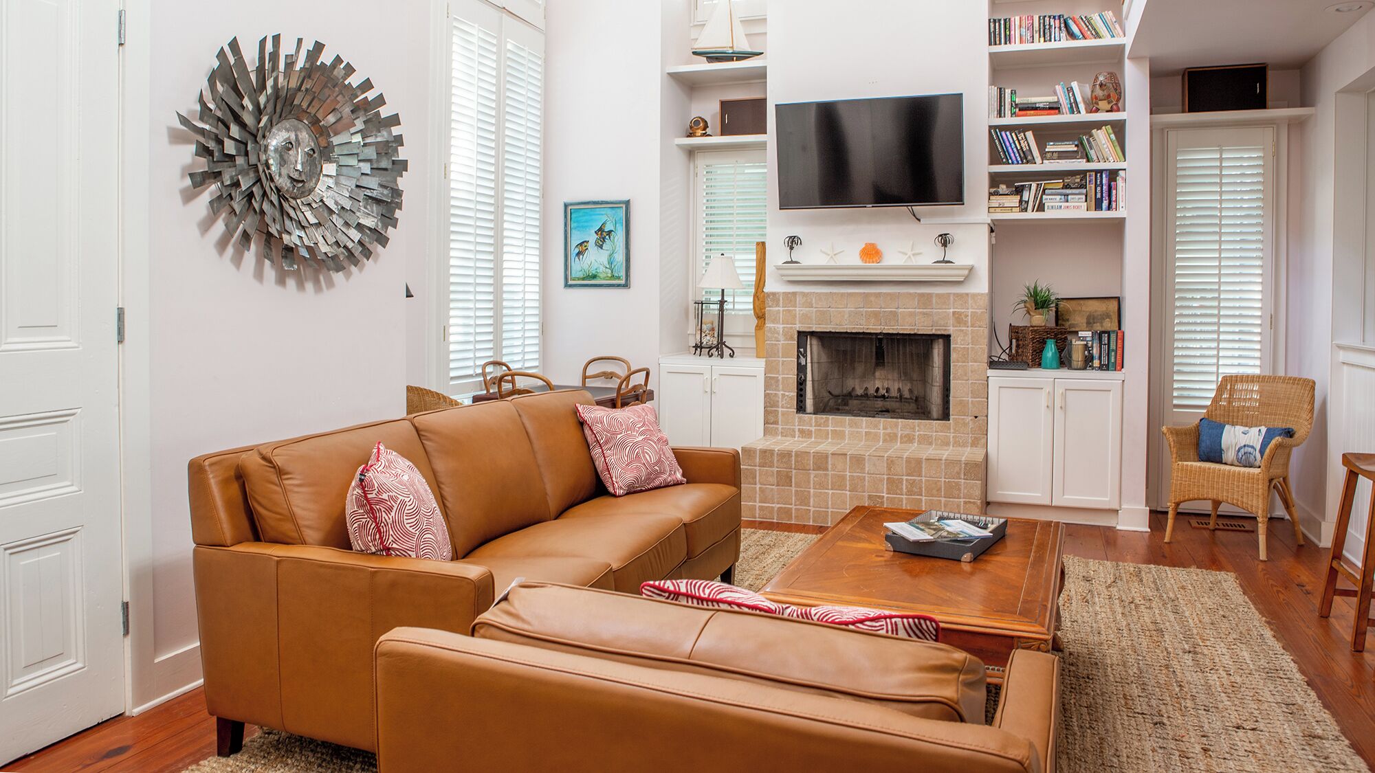 Uma sala de estar com um sofá de couro marrom, uma lareira, uma televisão e uma estante de livros.
