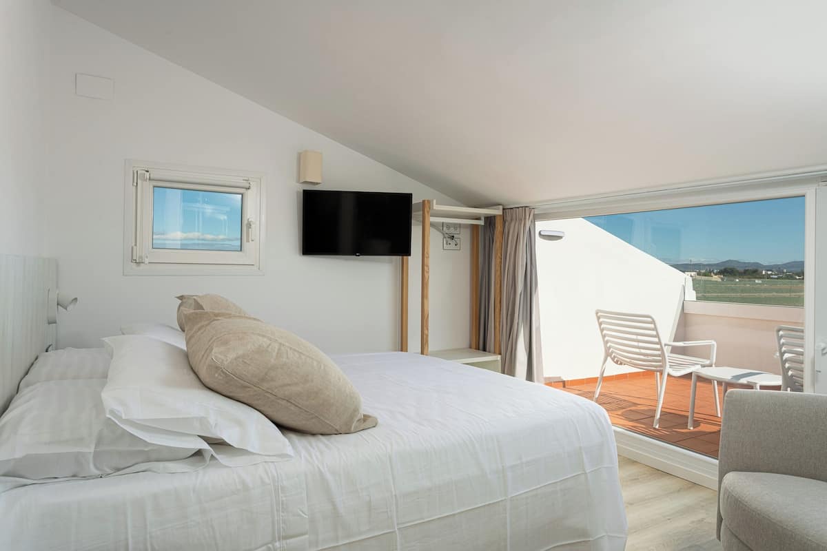Quarto com cama, televisão, janela e varanda com cadeiras.