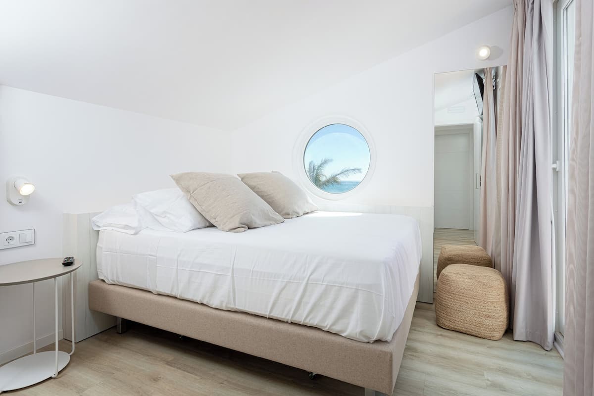 Quarto moderno com cama, mesa de cabeceira e janela com vista.