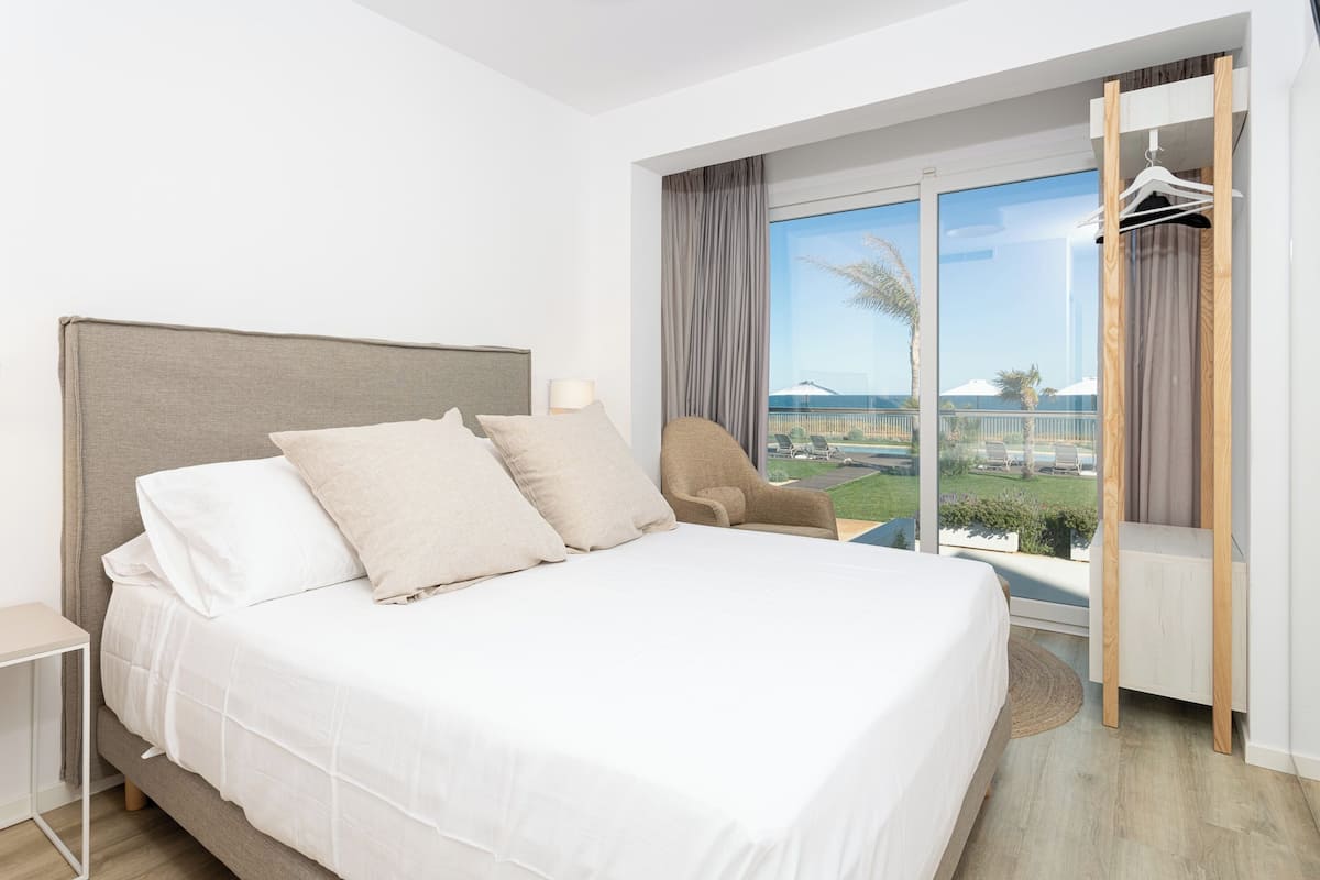 Quarto de hotel moderno com uma cama grande, uma cadeira, uma mesa e vista para o exterior.
