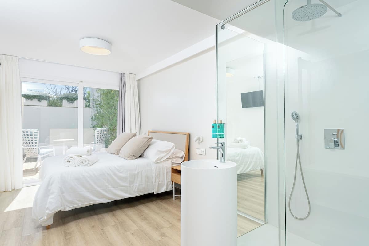 Quarto de hotel moderno com uma cama grande, box de chuveiro em vidro e vista para o exterior.