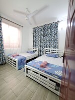 Quarto com duas camas de solteiro, ventoinha no teto e janela com cortinas.