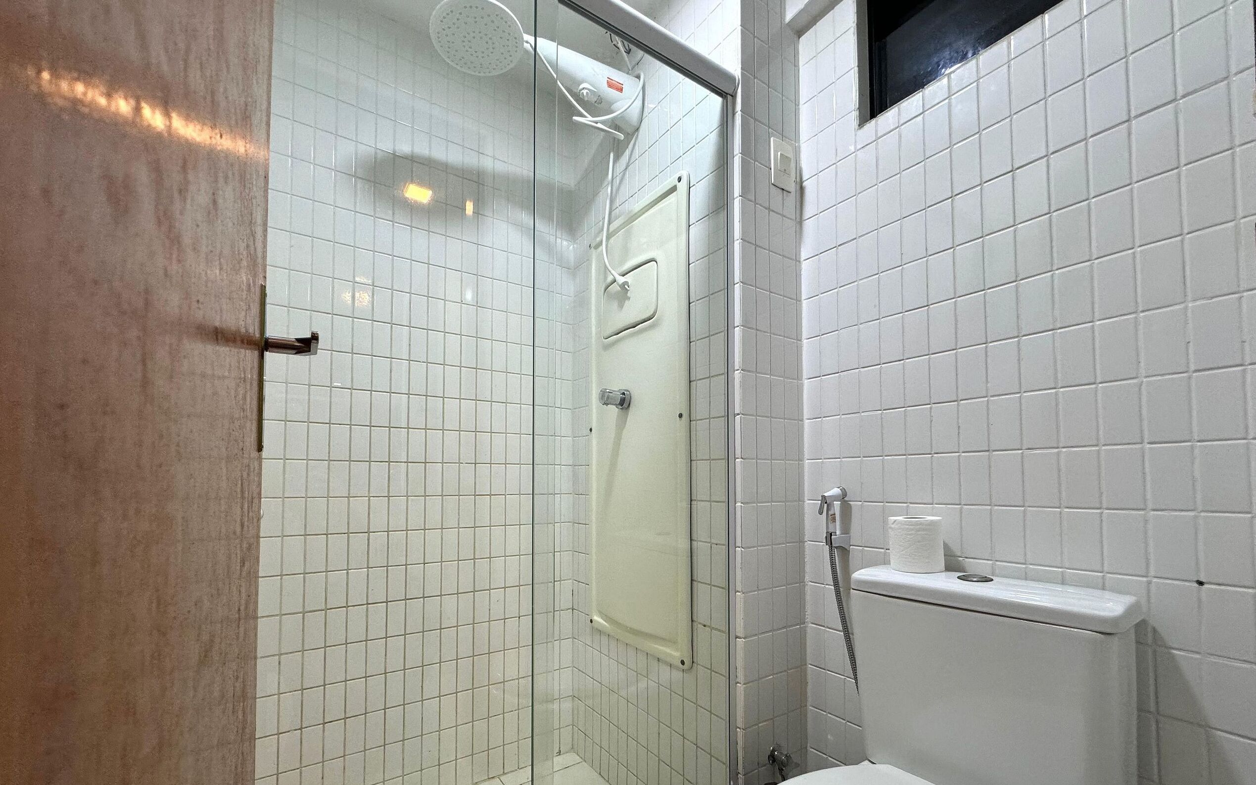 Um banheiro pequeno com azulejos, box de vidro, vaso sanitário e porta-toalhas.
