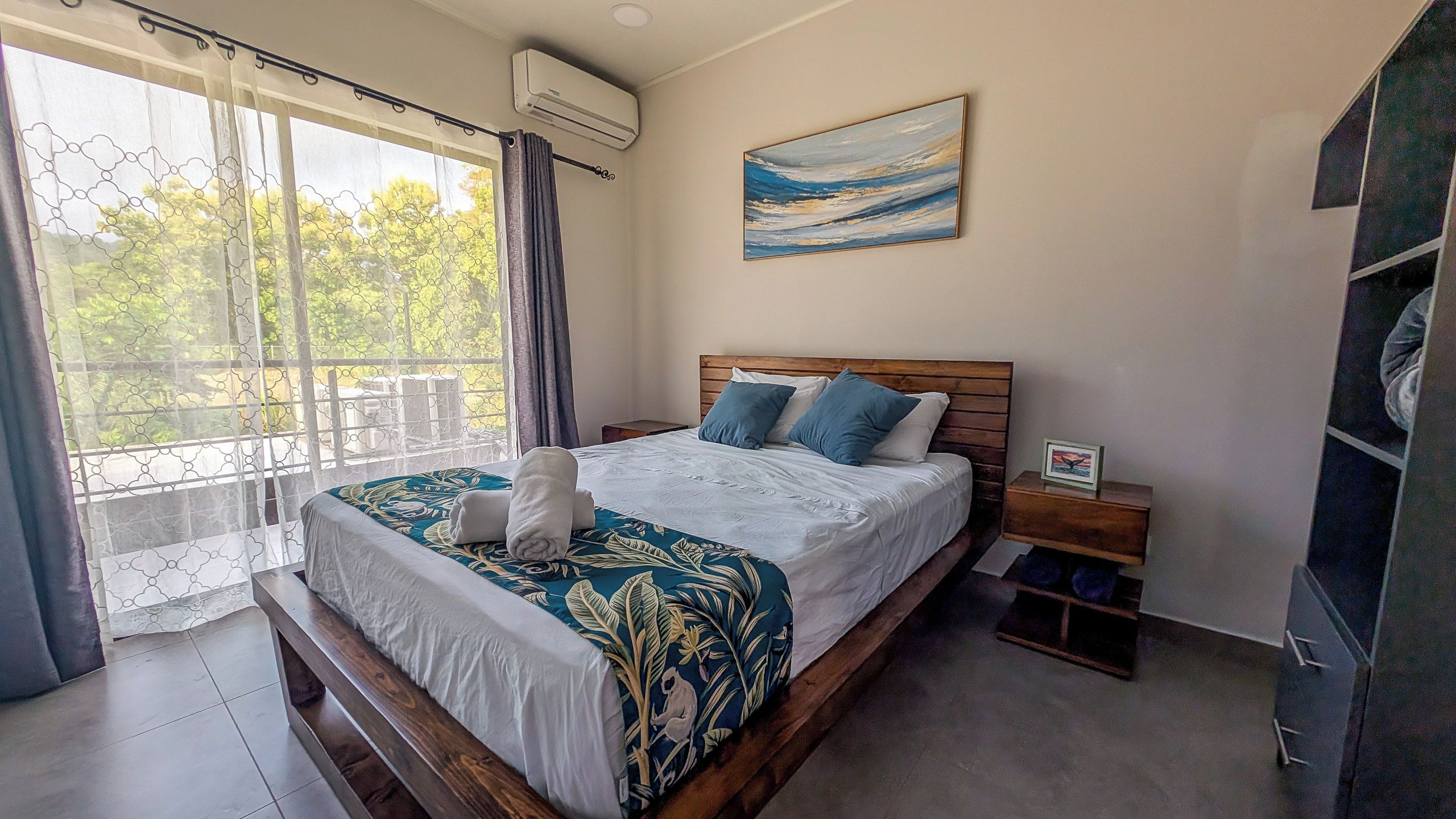 Quarto com cama, mesa de cabeceira, estante e janela com cortinas.