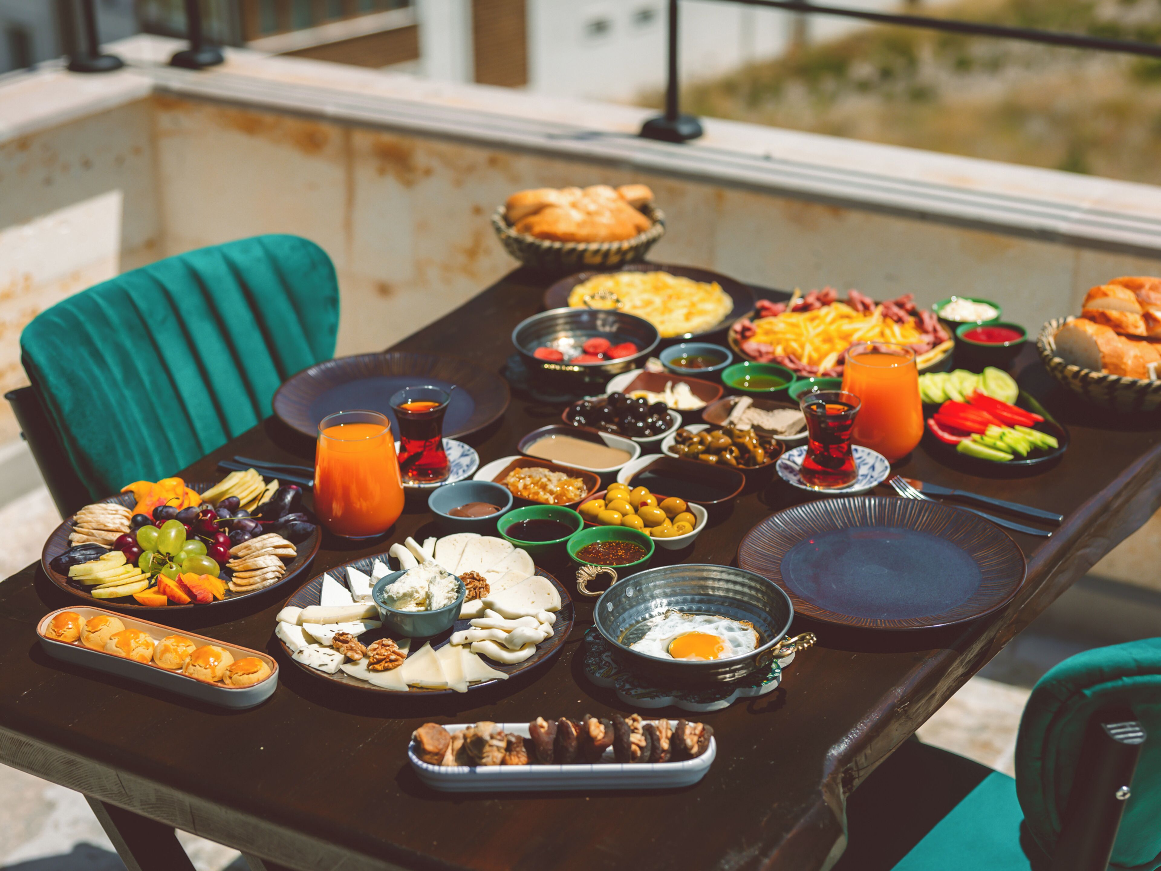 Uma mesa com diversos alimentos e bebidas, uma cadeira e um parapeito de varanda.