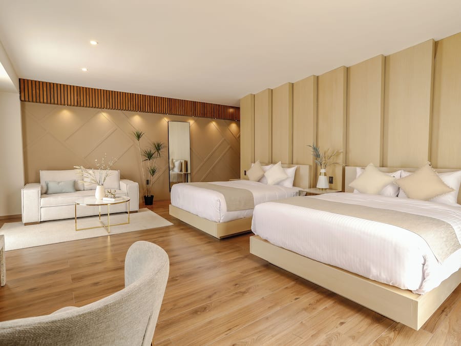 Quarto de hotel moderno com duas camas, um sofá, uma mesa de centro e um espelho grande.