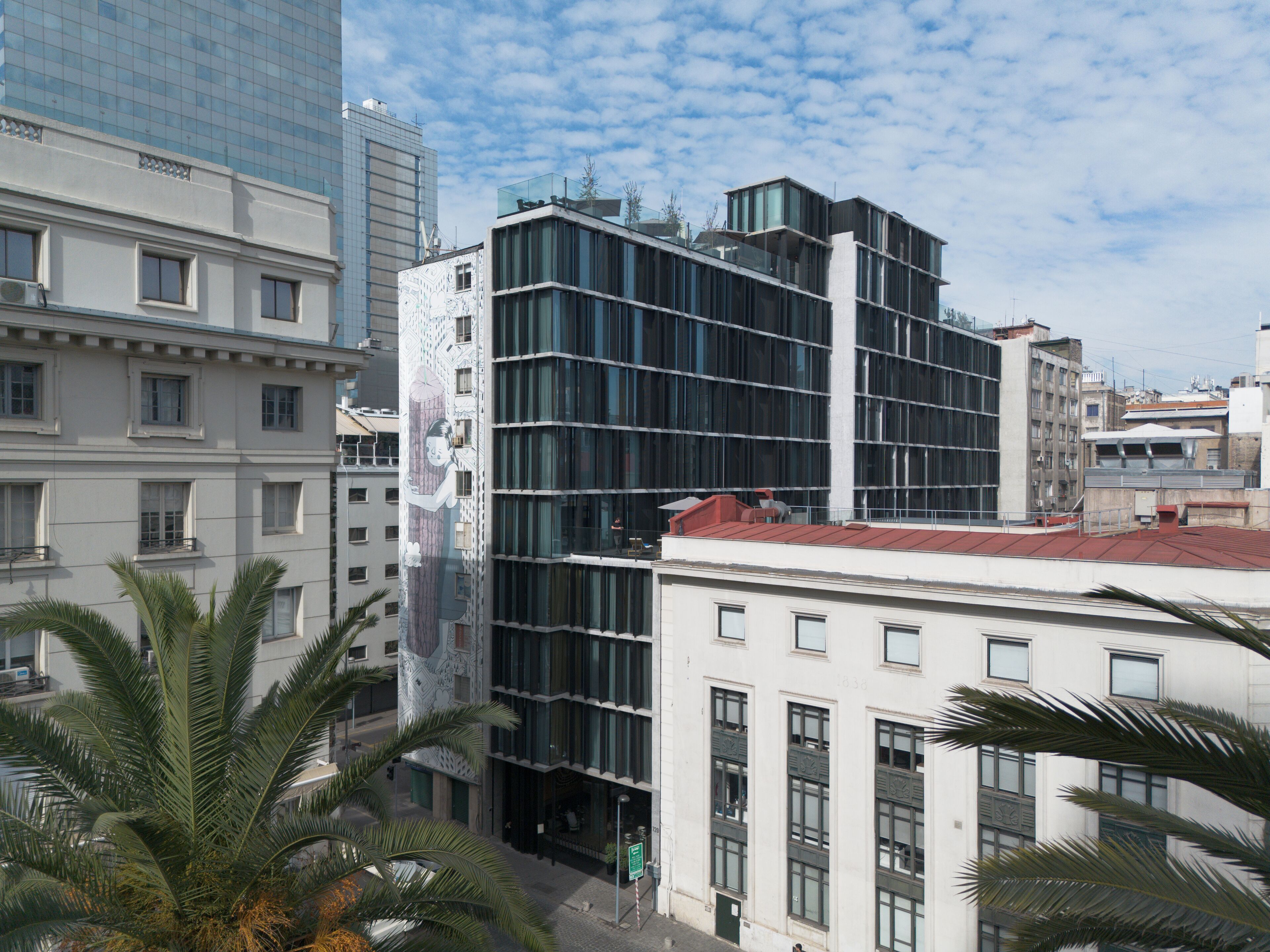 Um edifício moderno com fachada de vidro, cercado por palmeiras e outros edifícios.