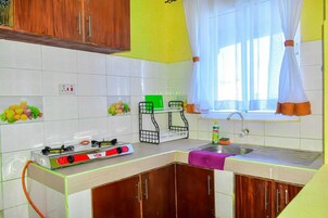 Uma cozinha com azulejos brancos, armários de madeira, fogão a gás, pia e uma janela com cortinas.