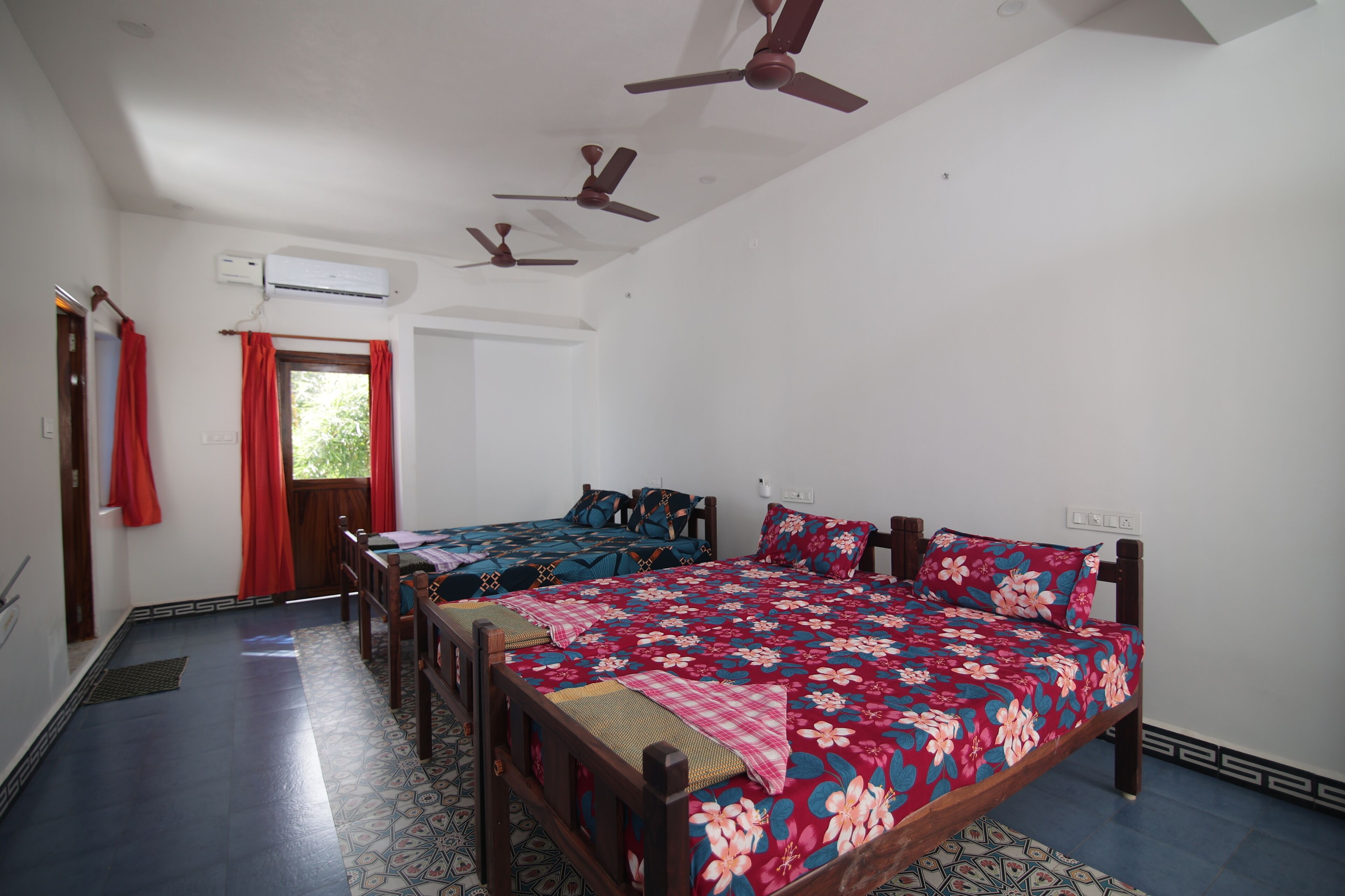 Quarto com duas camas de solteiro, piso de madeira e ventoinha no teto.