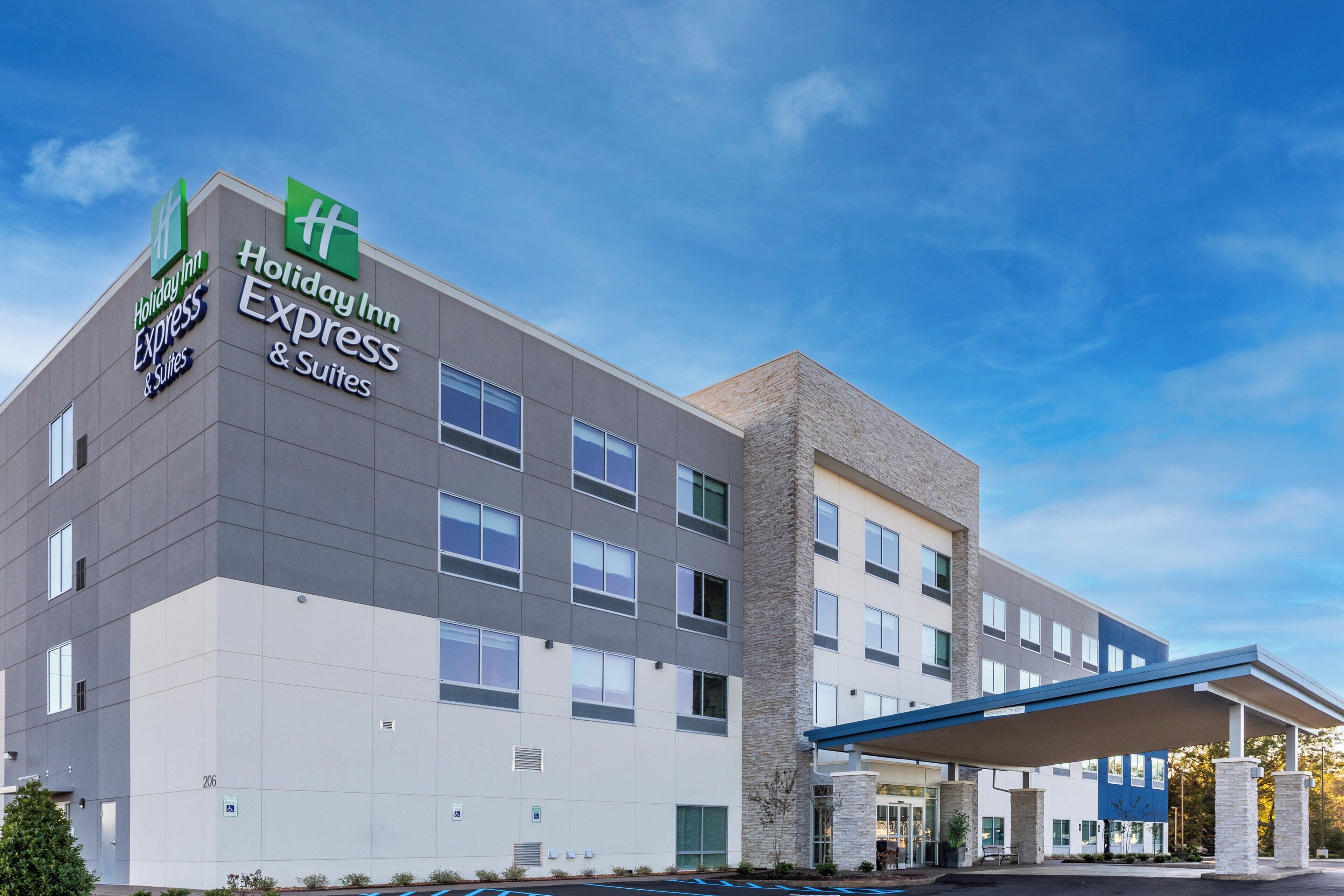 Edifício do Holiday Inn Express & Suites com design moderno, apresentando uma entrada coberta e estacionamento.
